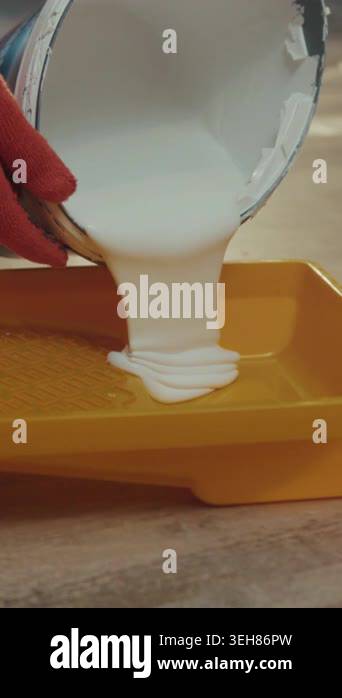 white paint pouring into yellow tray, steady stream from metal can ...