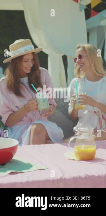 two friends sharing garden brunch and sipping juice from jars, pitcher ...