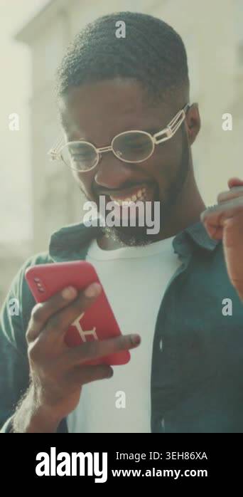 man laughing while reading phone on sunny street, golden light and ...
