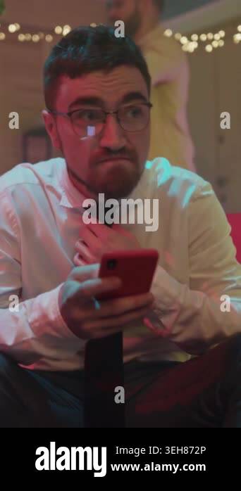 tired businessman in shirt and tie scrolling phone on red couch at ...