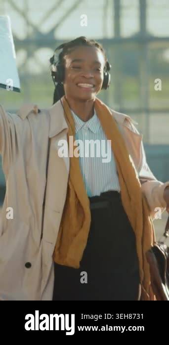 black woman dancing at transit terminal, trench coat and mustard scarf ...