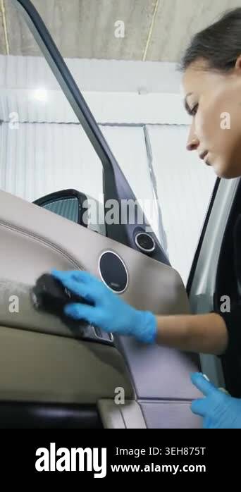 A woman is cleaning the inside of a car with a brush. She wears blue ...