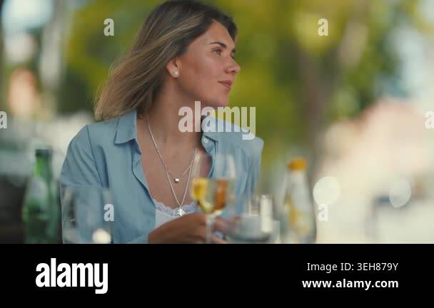 A woman sits at an outdoor cafe, looking around and enjoying her drinks ...