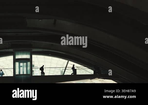 Groups of people walk along paths inside a modern structure. Light ...