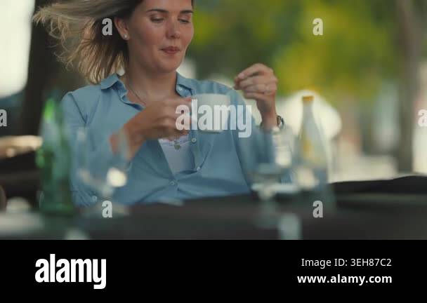 A woman sits at a cafe enjoying her coffee while stirring the cup ...