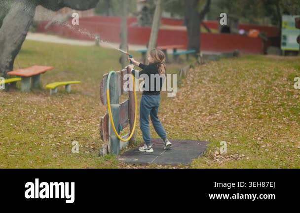A child enjoys spraying water from a hose in a park. There are trees ...