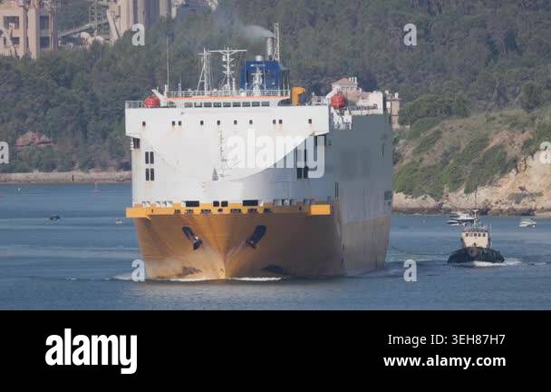 A large cargo ship is moving through the water with a tugboat assisting ...