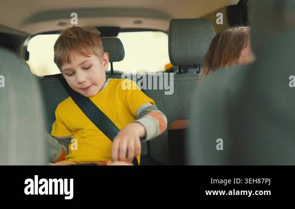 A young boy in a yellow shirt plays with toys in the back seat of a car ...