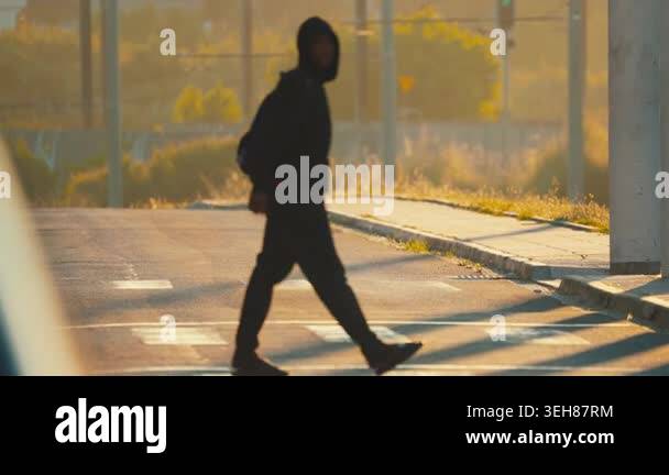 A person crosses the street in an urban area during sunset. The warm ...