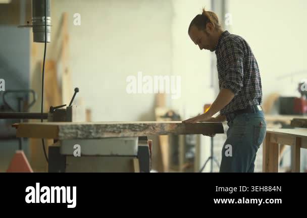 Male woodworker processing a raw wood plank on a jointer machine in his ...