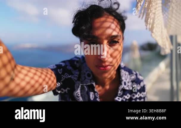 Young woman with curly dark hair takes selfie under woven net umbrella ...