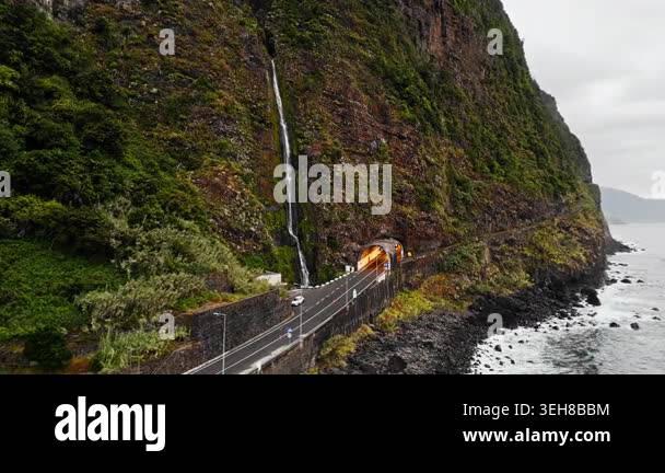 Cliff waterfall descending onto seaside road with tunnel on Madeira ...