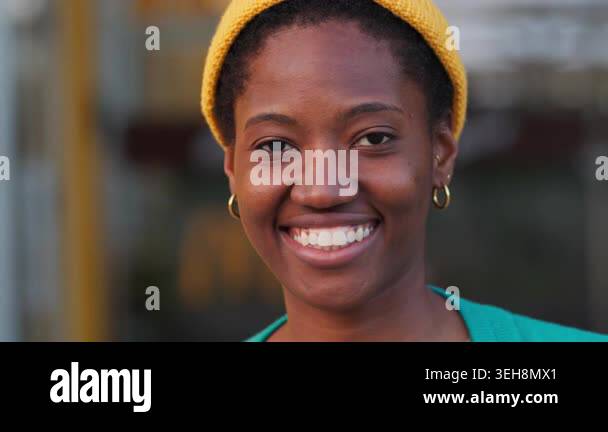 Smiling young black woman in yellow cap outdoors during daytime ...