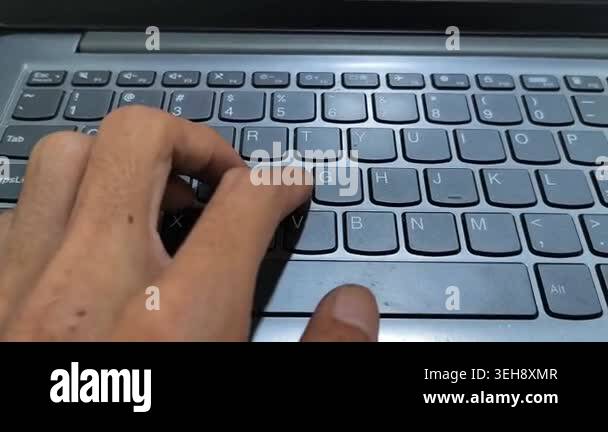 A man's hand is typing on a laptop keyboard while working at a wooden ...