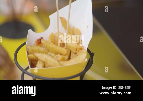 People eat fresh fries from a food stand outdoors in a lively area ...