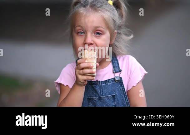 Little girl eating ice cream from waffle cone outdoors, wearing denim ...
