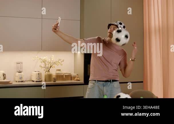 Young man in casual clothing captures a selfie while juggling soccer ...