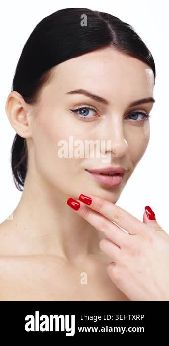 Young woman posing with red nails and a gentle smile while touching her ...