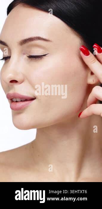 Woman applying skincare product on her face with closed eyes and red ...