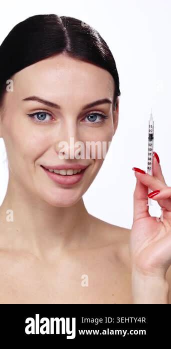 Smiling woman holding a syringe in one hand with a neutral expression ...
