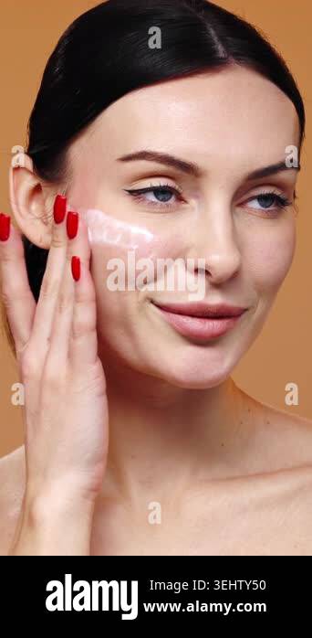 Young woman applying skincare product to her face with a smile against ...