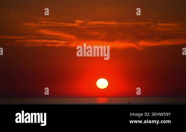 Stunning red sunset over calm sea with glowing sun and dramatic clouds ...