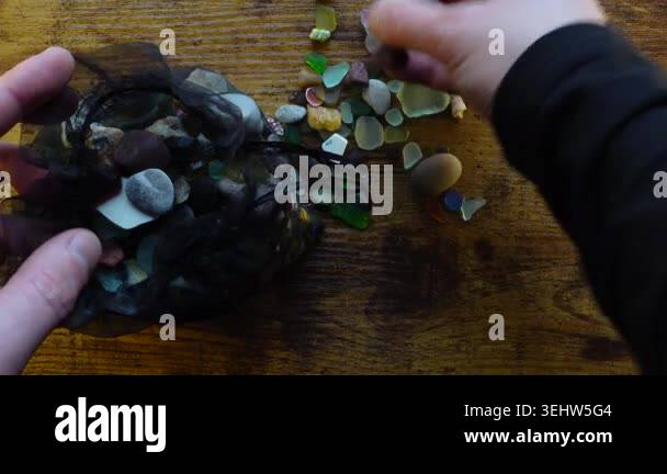 Hands picking and examining sea glass, shells and pebbles scattered on ...