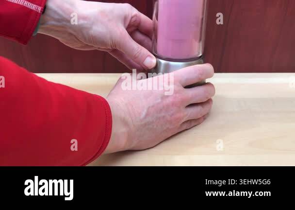 Making a strawberry milkshake in portable blender on wooden background ...