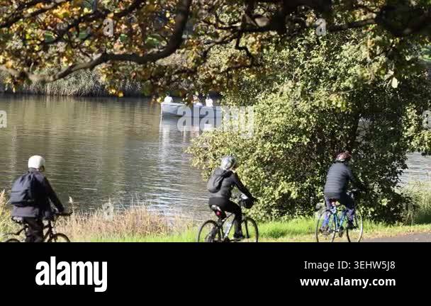Two cyclists riding bicycles along a scenic riverbank surrounded by ...