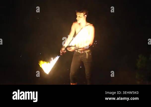 Young man performing fire tricks with fire torches in a dark outdoor ...