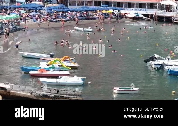 Numerous people swimming and relaxing in clear water at a crowded beach ...
