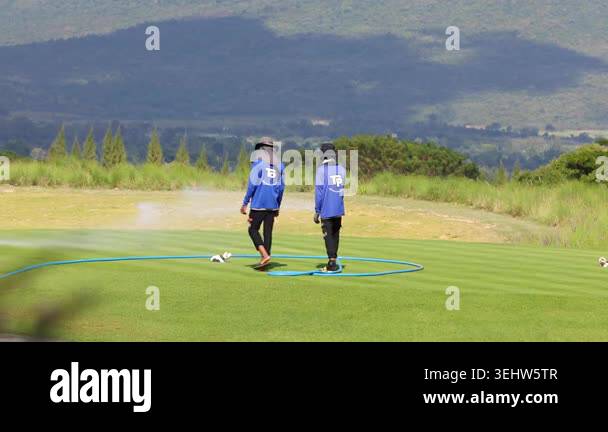 Two workers in blue jackets walking on a grassy field with mist and ...