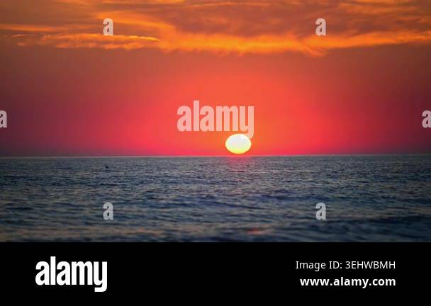 Fiery evening sky and glowing sun over calm ocean water, stunning ...