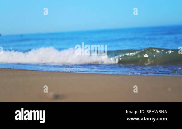Blue sea waves gently crashing on a sandy beach under clear summer sky ...