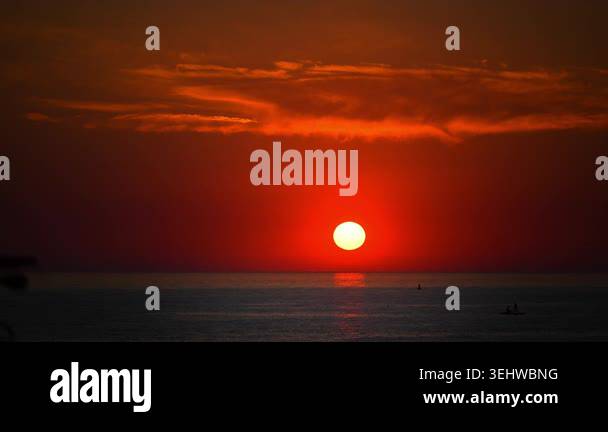 Glowing sun descending over calm ocean beneath dramatic clouds ...