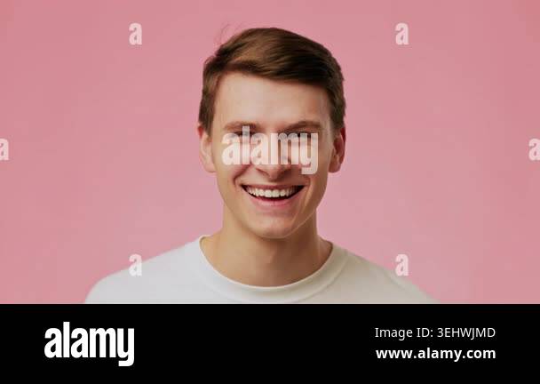 Young man with light skin is smiling joyfully in a studio with a pink ...