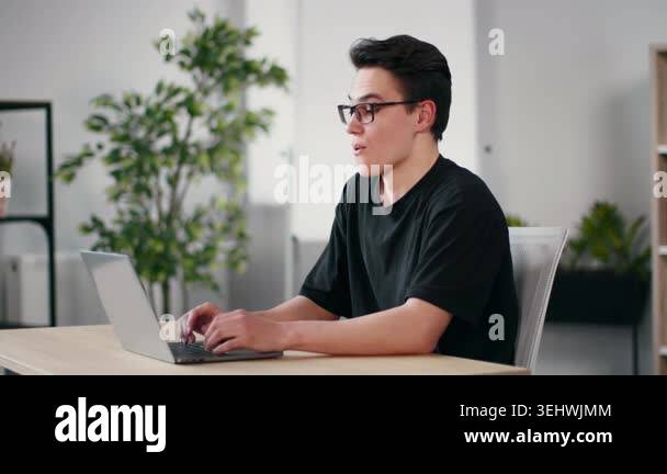 Young man with light skin is focused on his laptop while sitting at a ...