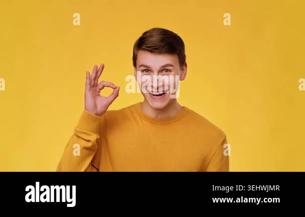 A young man with light skin smiles while making an okay gesture with ...