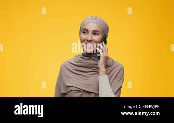 A woman with a headscarf smiles while talking on her phone. She stands ...