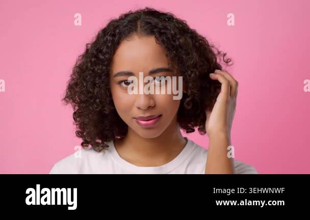 A young woman with curly hair and light skin poses confidently against ...