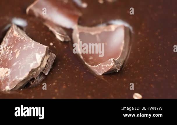 Dark chocolate pieces falling into liquid melted chocolate in slow ...