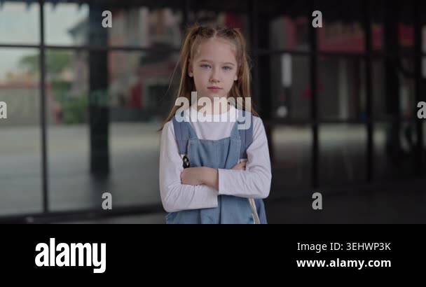 Portrait of calm little girl in denim overall stands near building with ...