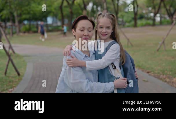 Portrait of loving mother hugs cute junior schoolgirl in spring park ...