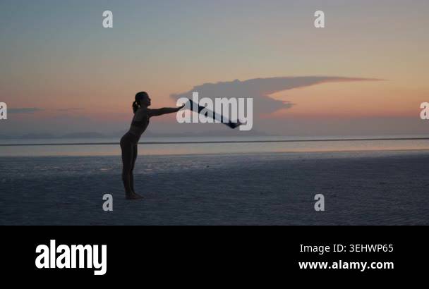 Silhouette of sportive woman lays yoga mat down on sea beach at sunrise ...