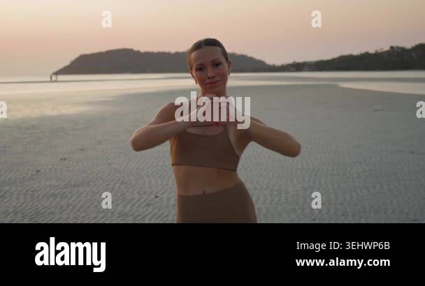 Portrait of cheerful woman in sports bra shows heart by hands as stands ...
