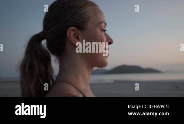 Portrait of beautiful woman with ponytail looks at ocean from sunrise ...