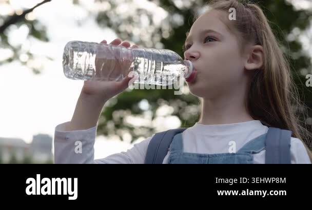 Portrait of thirsty little girl with backpack drinks water from plastic ...