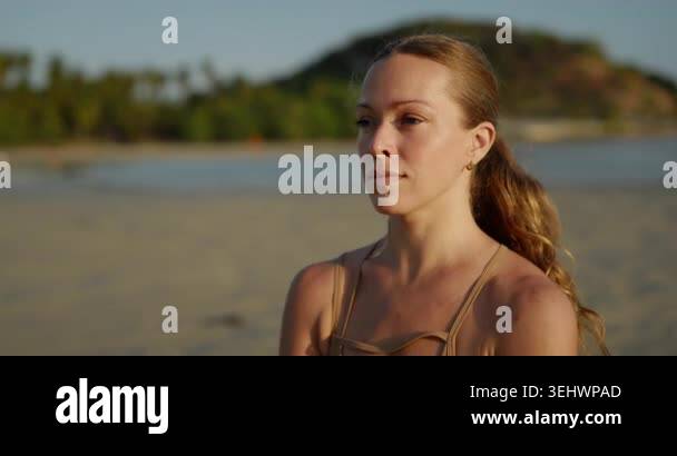 Portrait of tranquil young woman raises arms and closes eyes on sunrise ...