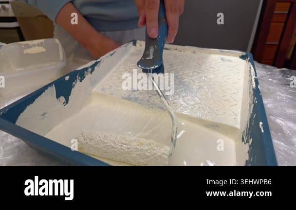 Person rolling white paint on roller in paint tray on covered ...