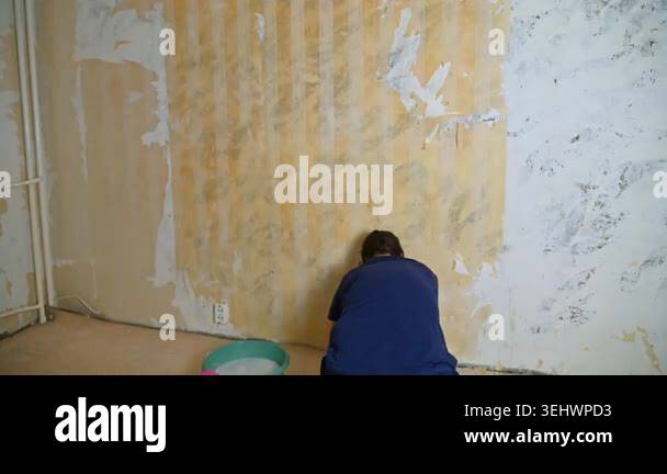 Woman scraping wallpaper off interior wall during home renovation in ...